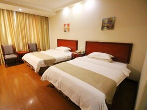 Quarto de hotel com duas camas, uma cadeira, uma mesinha e uma mesa de cabeceira.