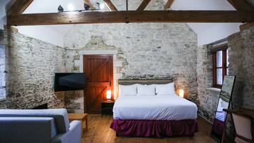 Um quarto rústico com parede de pedra, vigas de madeira, cama com roupa de cama branca, uma TV e um quadro na parede.
