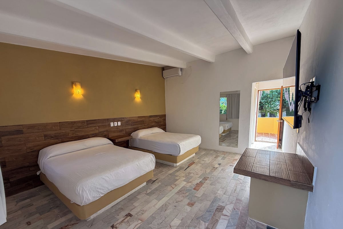 Quarto de hotel com duas camas, uma cabeceira de madeira, uma mesinha de madeira e um espelho.