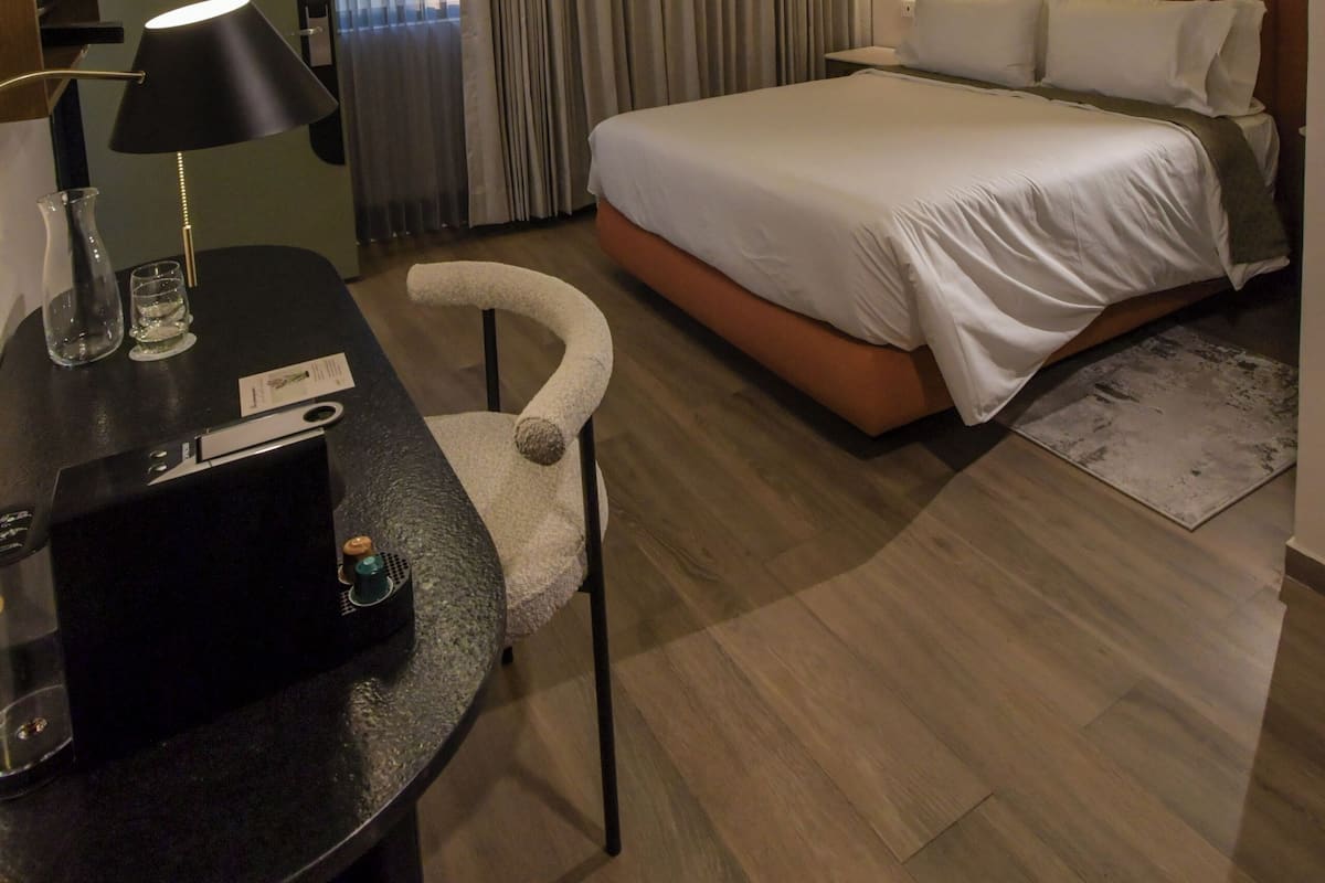 Quarto de hotel com cama, escrivaninha com luminária, cadeira e mesa de cabeceira.