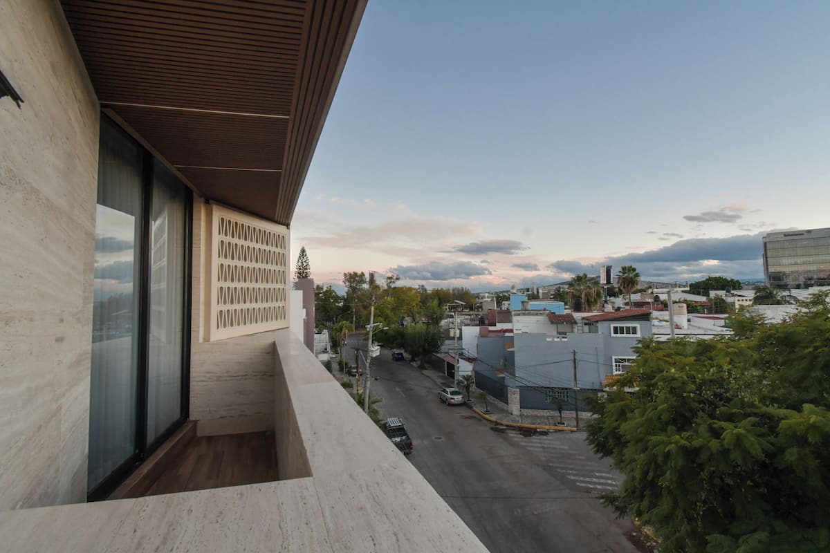 Um edifício moderno com grandes janelas e varanda com vista para uma rua com carros e edifícios.