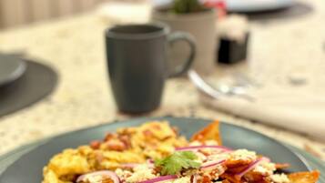 Um prato de nachos com acompanhamentos, uma caneca cinza e uma planta em vasos ao fundo.