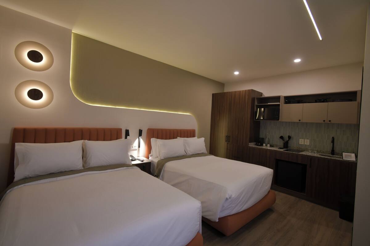 Quarto de hotel moderno com duas camas, cozinha planejada e design de teto original.