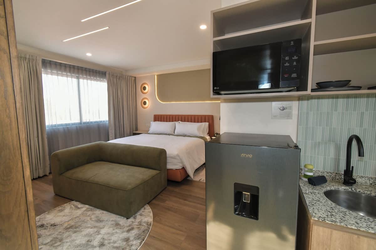 Quarto de hotel compacto com cama, sofá, cozinha compacta com micro-ondas e pia.