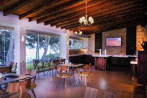 Um interior moderno com vigas de madeira no teto, uma área de bar com televisão e um espaço de refeições com cadeiras e mesas.