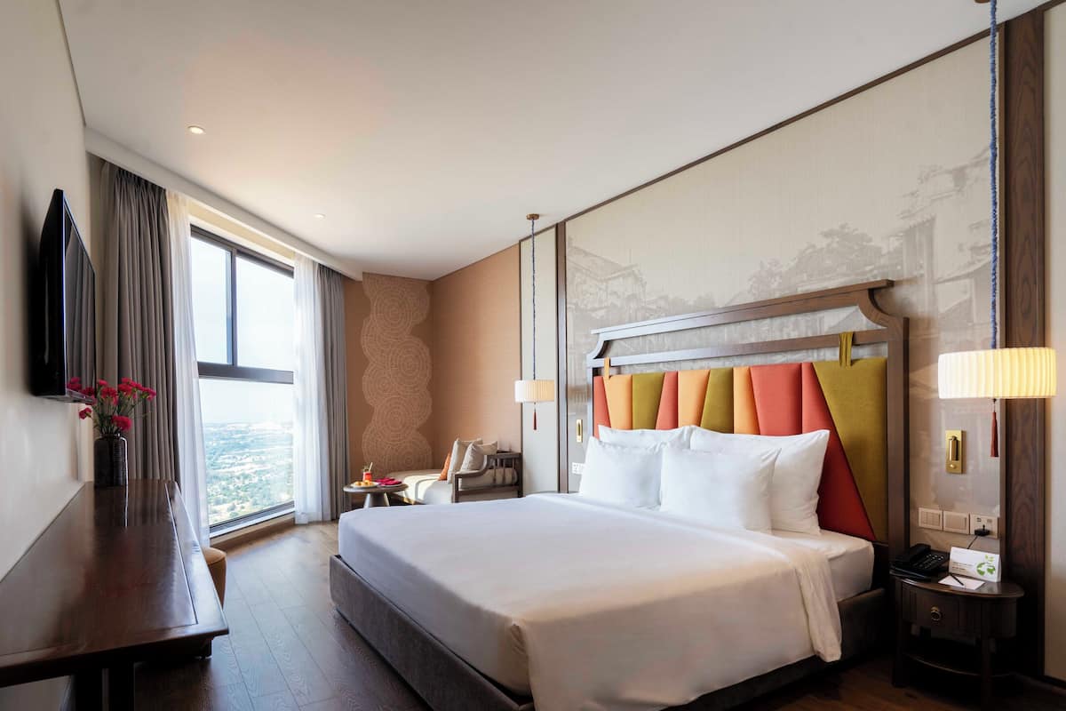 Quarto de hotel com uma cama grande, uma escrivaninha, uma cadeira, uma televisão e uma janela com vista.