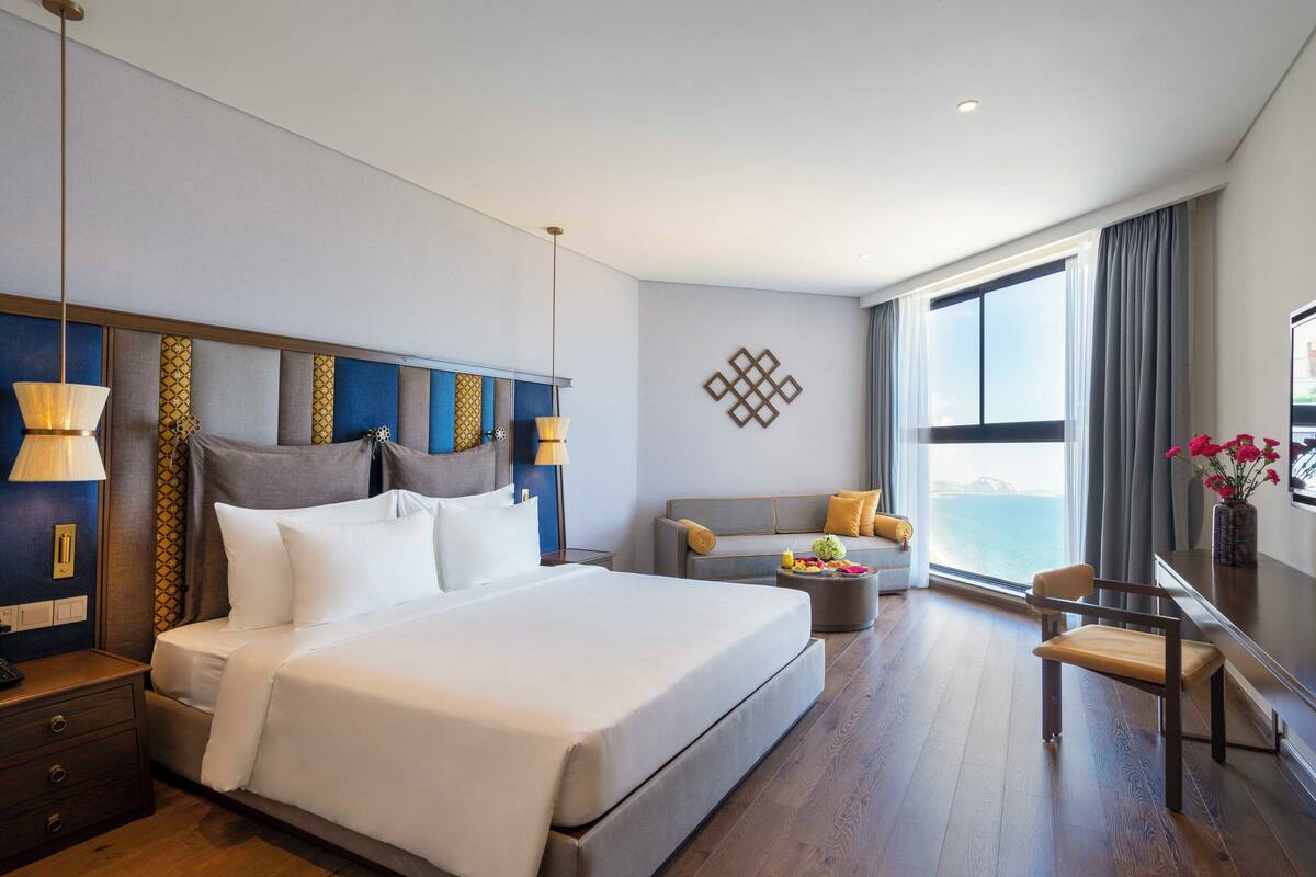 Quarto de hotel com uma cama grande, um sofá, uma mesa de jantar e vista para o mar.