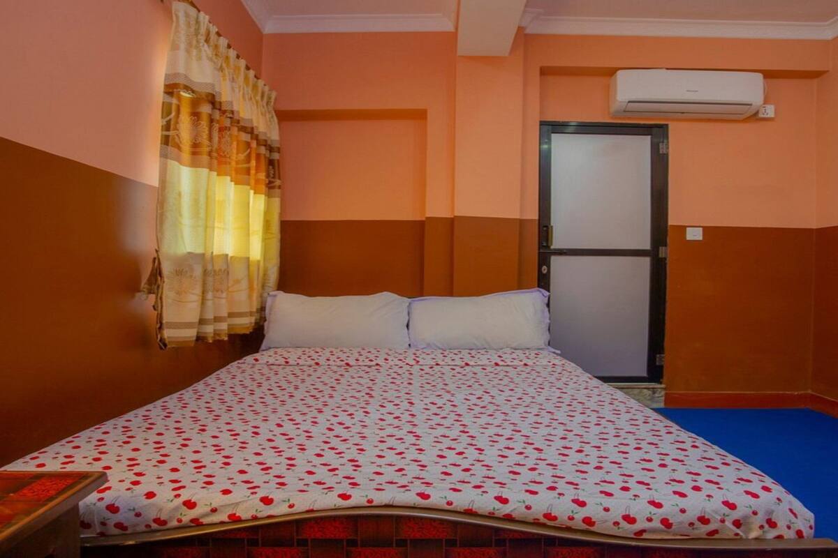 Quarto de hotel com cama, janela com cortinas, aparelho de ar condicionado e tapete azul.