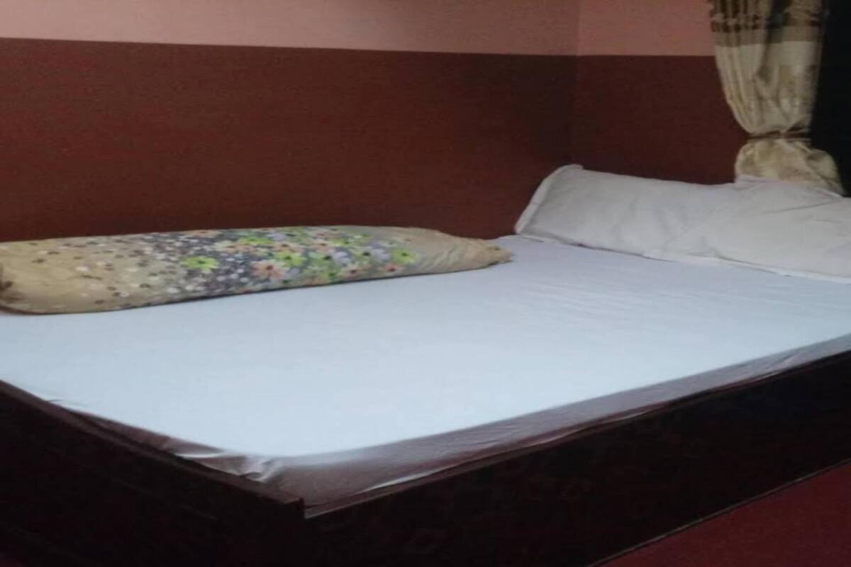 Uma cama de solteiro com travesseiro estampado e lençóis brancos em quarto com parede vermelha e marrom.