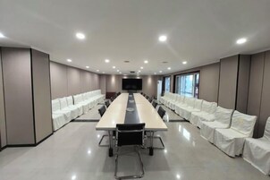 Uma sala de conferências com uma mesa comprida, cadeiras e assentos cobertos por toalhas brancas em ambos os lados.