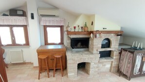 Uma cozinha acolhedora com lareira de pedra, banquetas de madeira e uma janela com cortina decorativa.