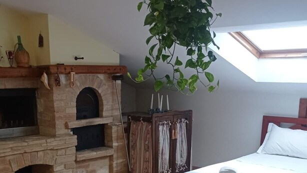 Um quarto acolhedor com lareira de pedra, uma mesa de jantar com garrafa de vinho e limões, cama com lençóis brancos e uma planta pendente.