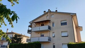 Um edifício residencial com vários andares, varandas, um telhado plano e céu claro.