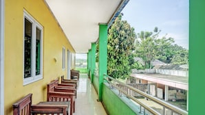 Um corredor com bancos de madeira, pilares verdes e vista para áreas verdes e edifícios.