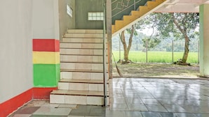 Uma escadaria com piso de azulejos leva a um espaço coberto, com vista para um campo verde e árvores.