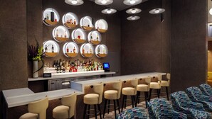 Uma área de bar com minibar, várias luminárias esféricas pendentes e banquetas.