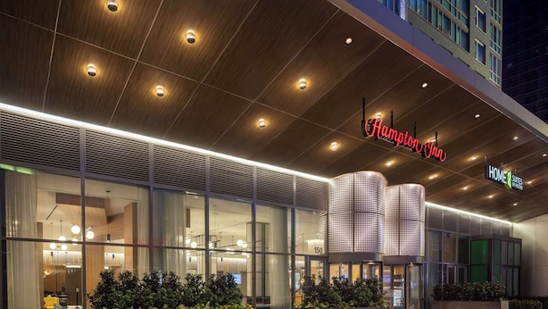 Entrada moderna de um hotel com uma grande placa indicando "Hampton Inn" e "Lar das Cidades por Avião".