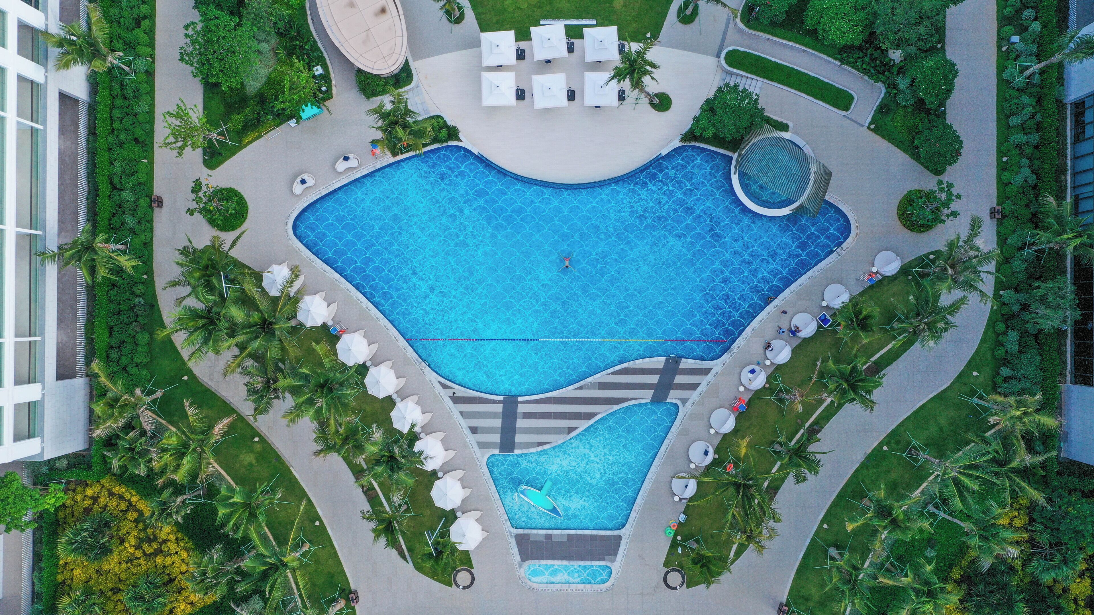 Vista aérea de um hotel com uma grande piscina central, várias piscinas menores e palmeiras ao redor.