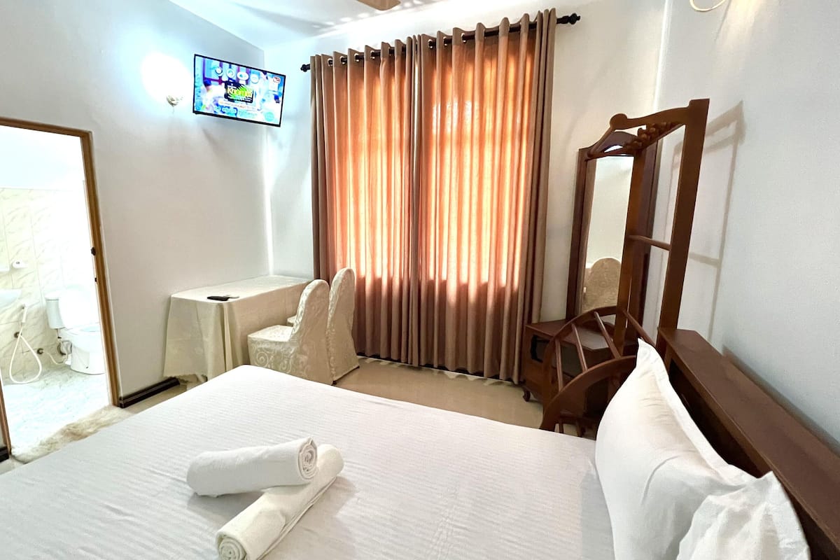 Quarto de hotel com uma cama, uma cadeira, uma televisão e cortinas.
