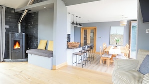 Uma sala de estar moderna com lareira, uma área de jantar com mesa e cadeiras de madeira, e um sofá com almofadas.