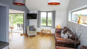 Uma sala de estar moderna com uma janela grande, uma televisão de tela plana, um sofá de couro marrom, uma poltrona estampada e uma mesa de centro de madeira.