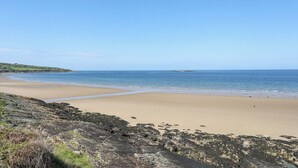 Uma praia com um primeiro plano rochoso e uma vista clara do mar.