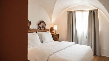 Quarto com uma cama grande, cabeceira de madeira, mesa de cabeceira com abajur e janela com cortinas.