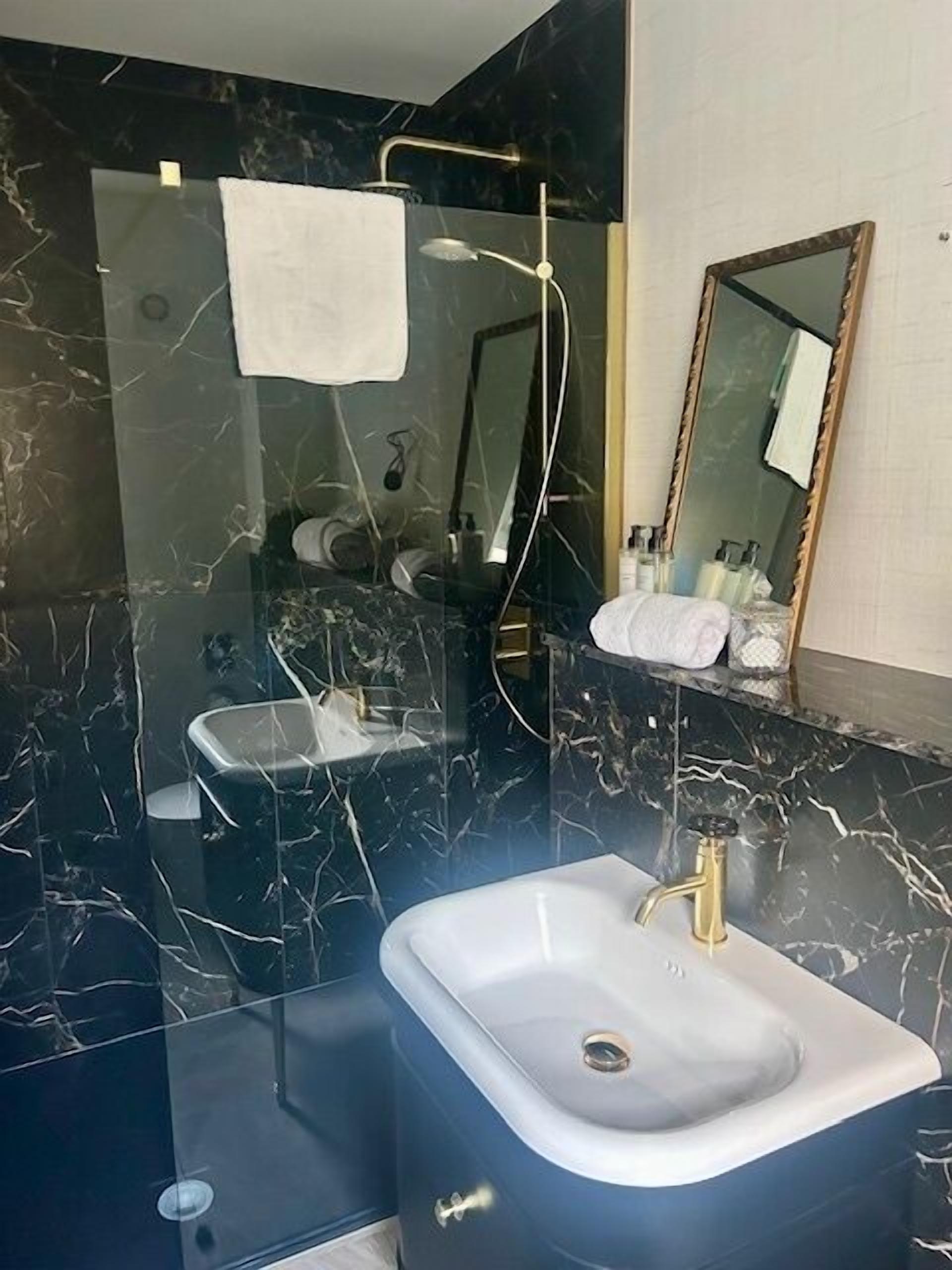 Uma casa de banho com lavatório de mármore preto, cabine de duche envidraçada e um espelho grande.