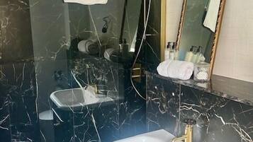 Uma casa de banho com lavatório de mármore preto, cabine de duche envidraçada e um espelho grande.