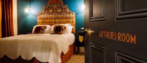Quarto com cama, cabeceira, mesa de cabeceira e porta com a inscrição "ARTHUR'S ROOM".