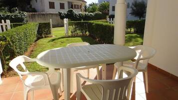 Pátio com mesa redonda e quatro cadeiras, cercado por um muro branco e vegetação.