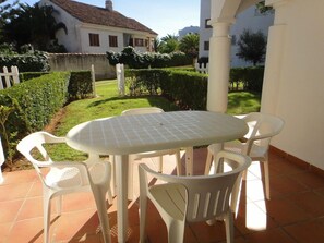 Pátio com mesa redonda e quatro cadeiras, cercado por um muro branco e vegetação.