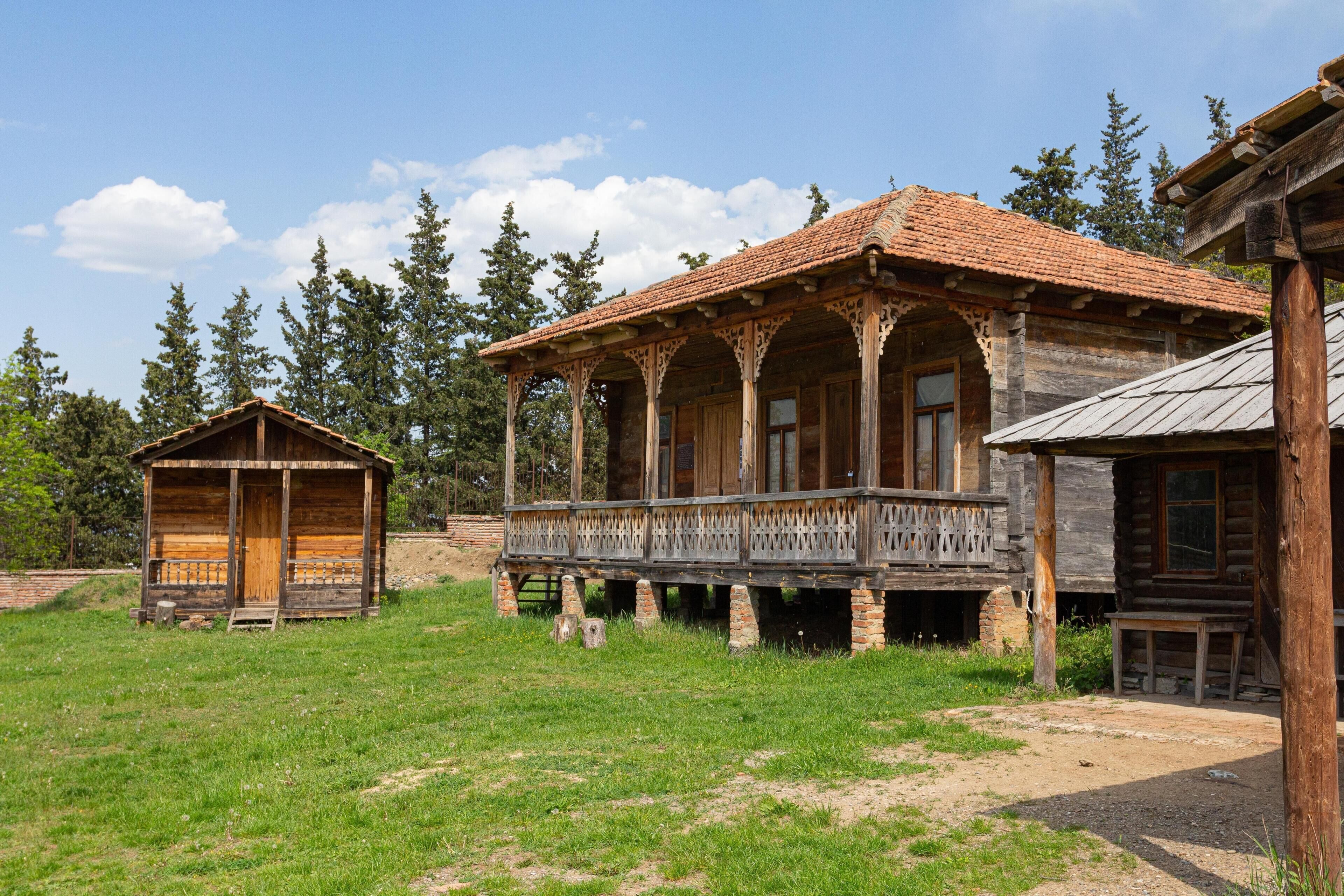 Uma cabana de madeira rústica com varanda, cercada por gramado e árvores.