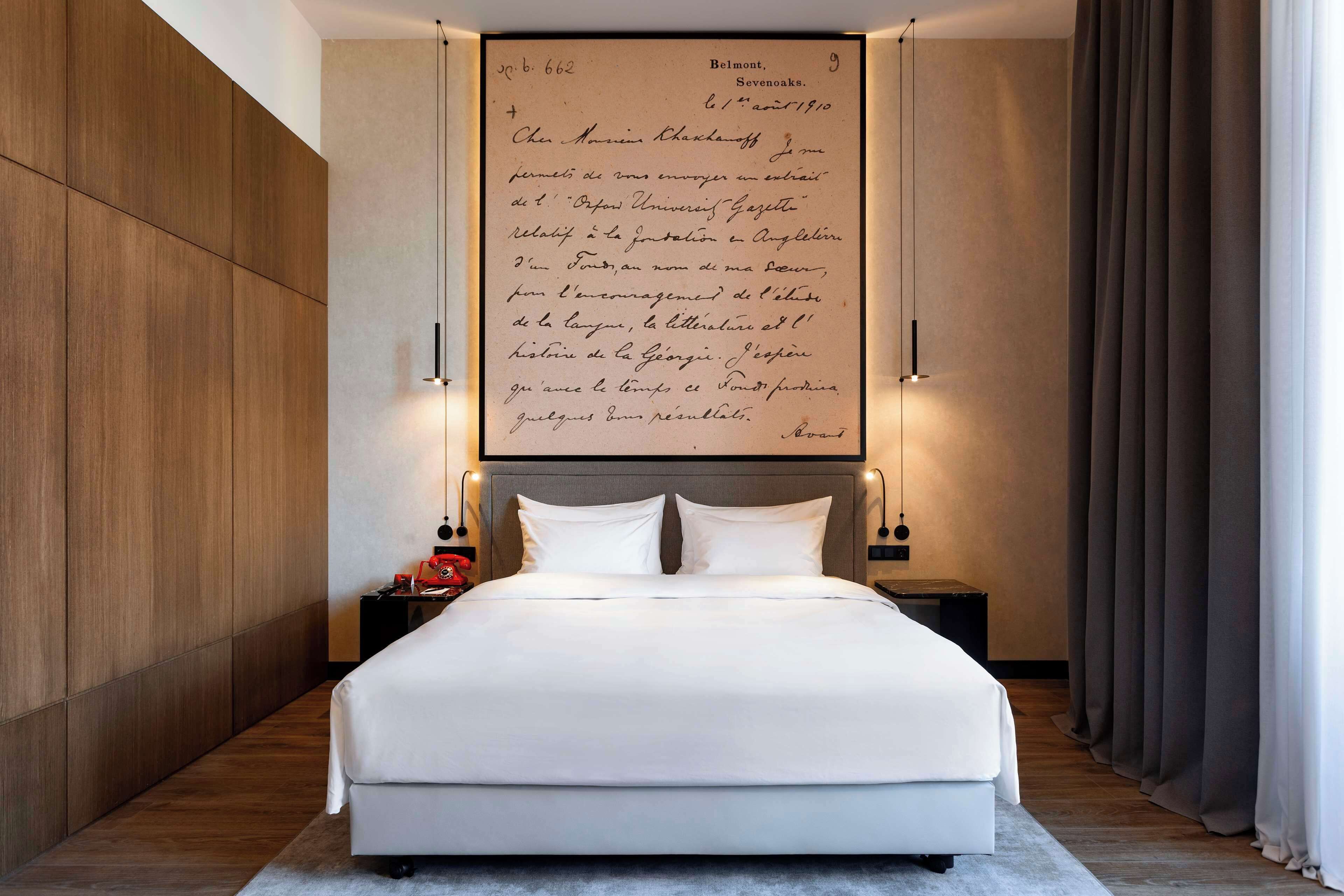 Quarto moderno com uma cama grande, lambris de madeira nas paredes e um texto emoldurado de grandes dimensões na parede.