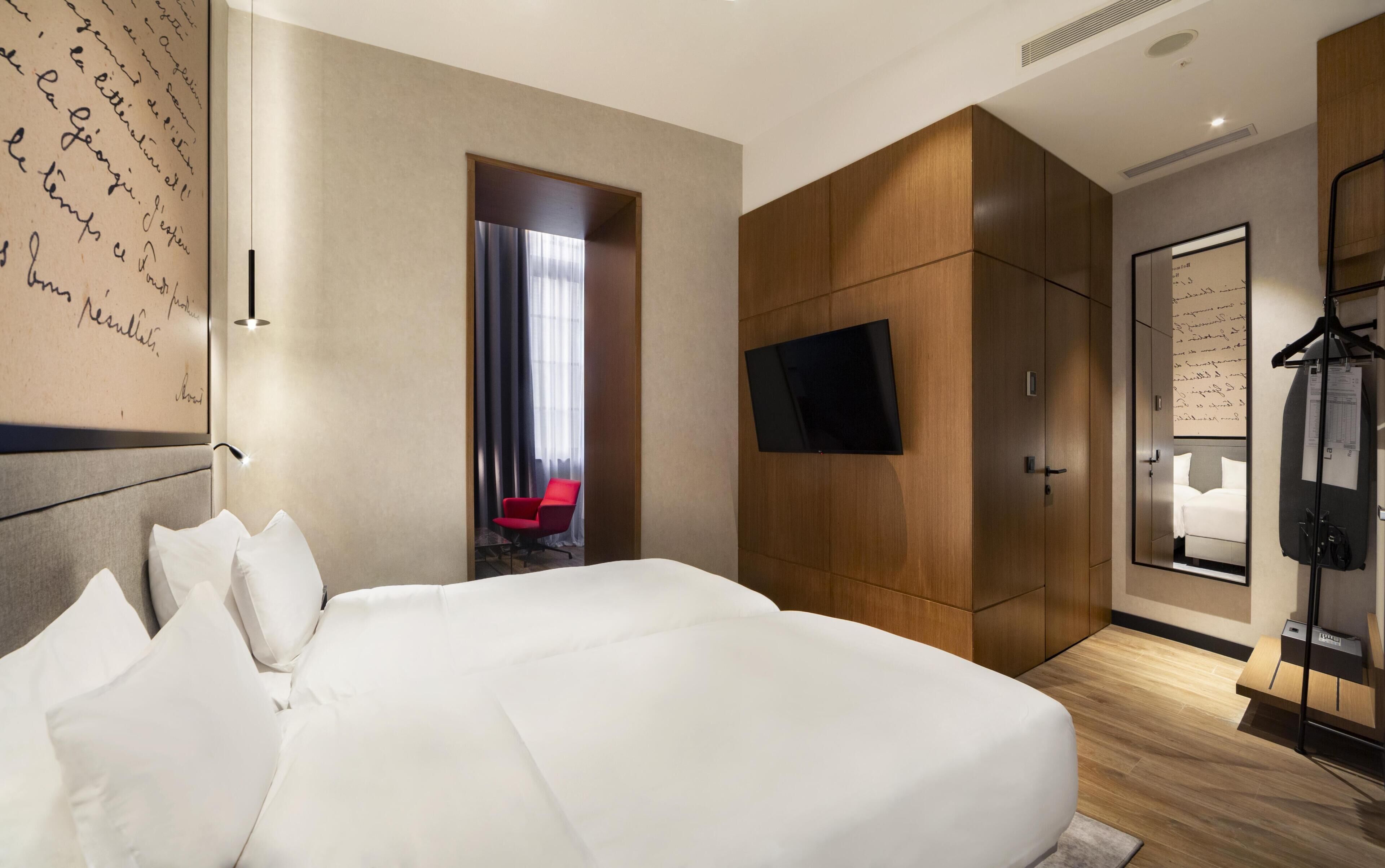 Quarto de hotel moderno com uma cama grande, televisão de tela plana, armário de madeira e um espelho com um bilhete.