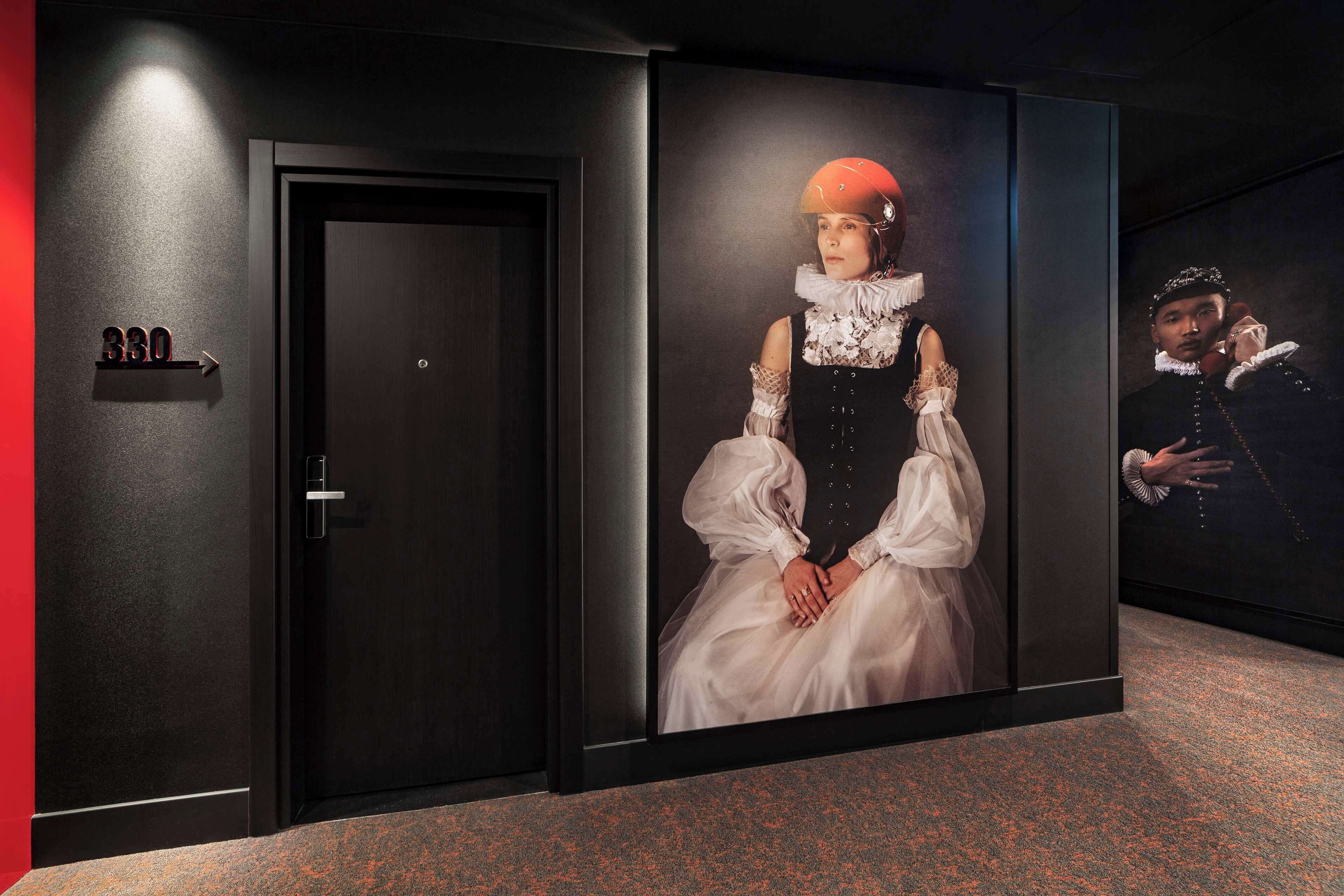 Um corredor com uma porta escura identificada com o número "330" e um retrato grande emoldurado de uma pessoa com vestes históricas.