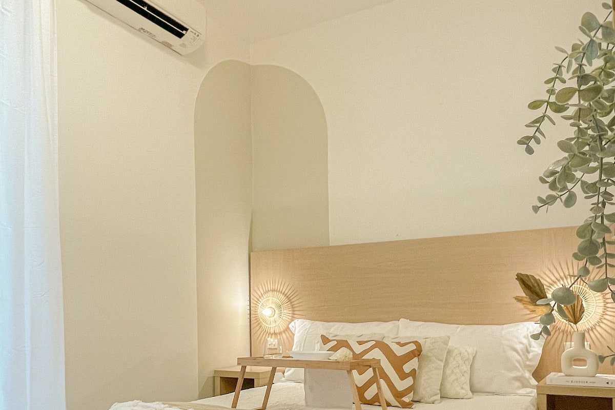 Quarto com cama, mesas de cabeceira, planta pendente e ar condicionado.