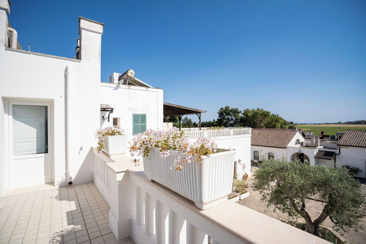 Edifício branco com varanda em azulejos e um vaso de flores.