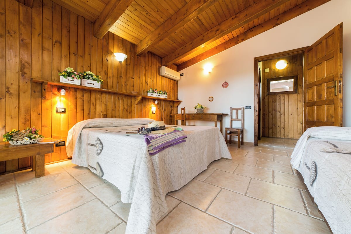 Quarto de madeira com duas camas, uma mesa e prateleiras com flores.
