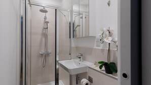 Uma casa de banho moderna com cabine de duche em vidro, uma sanita branca e um espelho sobre ela.