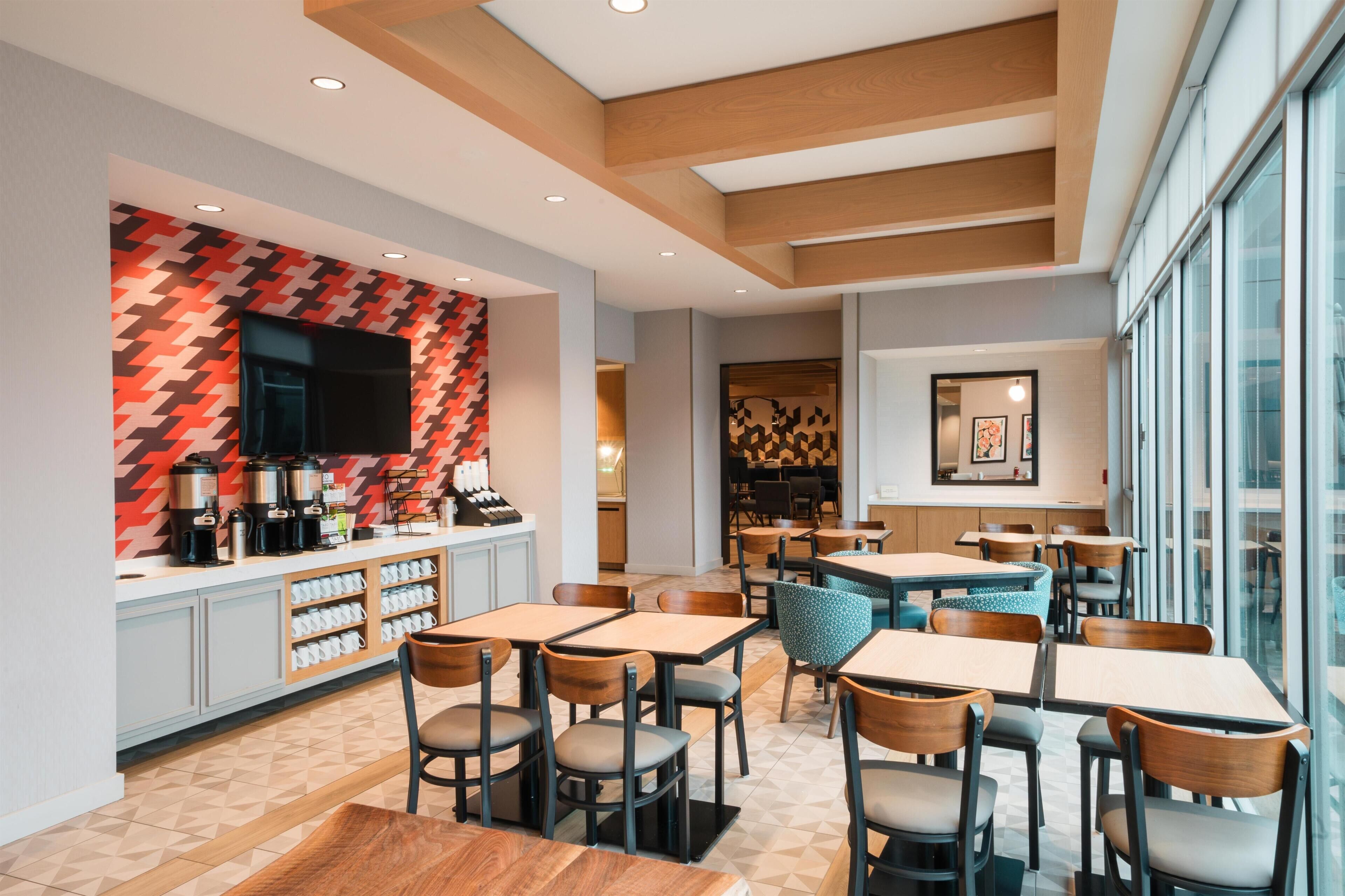 Um café moderno com parede em padrão herringbone, estação de café e mistura de cadeiras de madeira e estofadas.