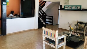 Uma área de recepção com balcão, escada e sala de estar com mesa de centro e livros.