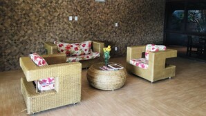 Um quarto com móveis de vime, incluindo um sofá e duas poltronas, uma mesa de centro redonda e um vaso decorativo com flores.