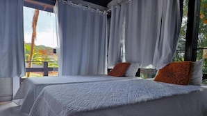 Quarto com duas camas, roupa de cama branca e vista para o verde lá fora.
