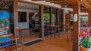Amplo espaço interno com piso de madeira, escada e área de refeições com mesas e cadeiras.