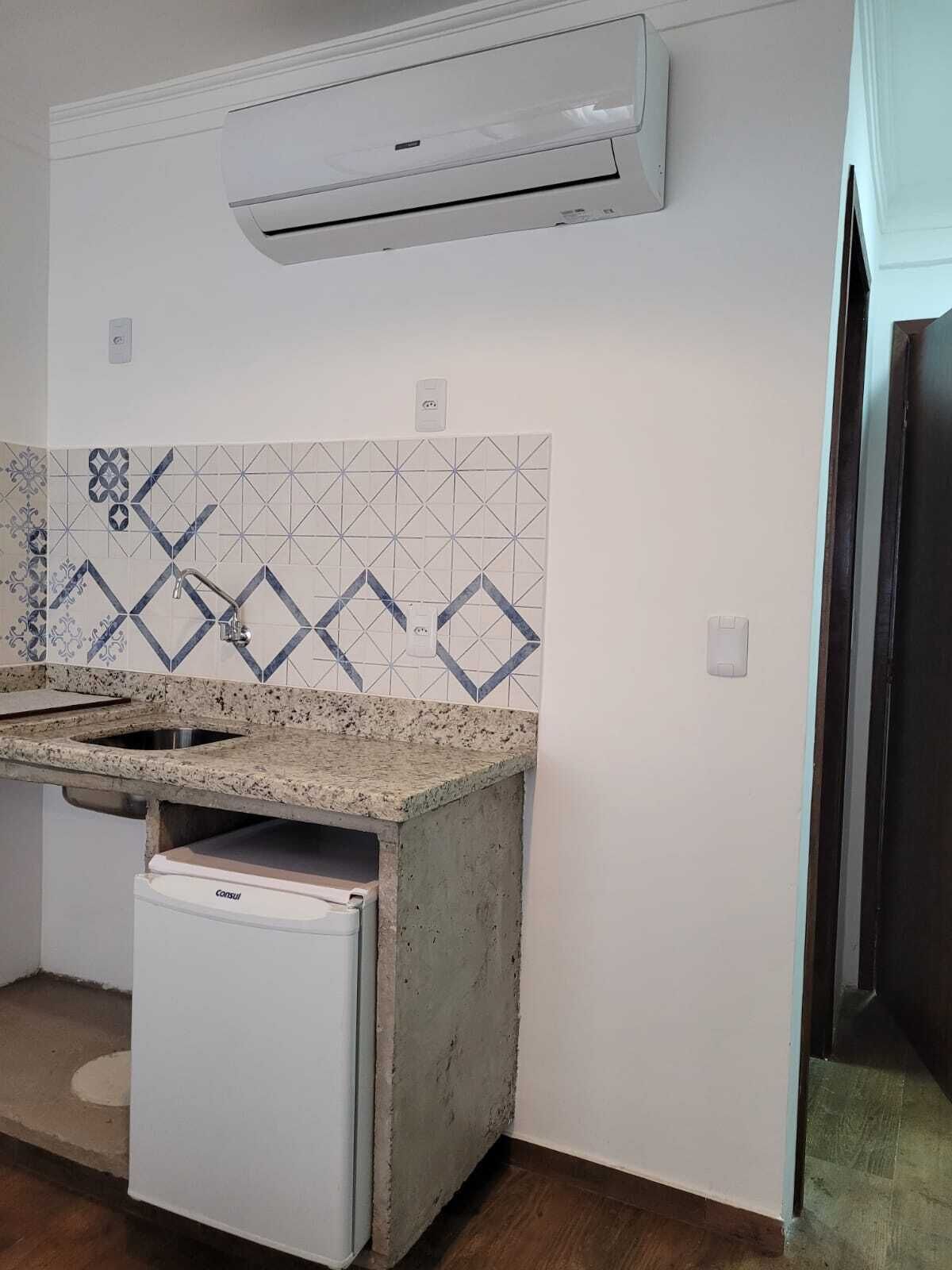 Cozinha com máquina de lavar louça embutida, painel de azulejos e ar condicionado fixado na parede.