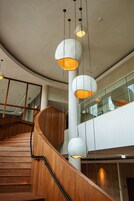 Um interior moderno com uma escada em curva, corrimãos de madeira e iluminação pendente.