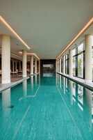 Uma piscina interior extensa com água cristalina, cercada por colunas e grandes janelas.