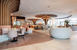 Um hall de hotel moderno com área de estar central, um bar e uma peça decorativa branca grande.