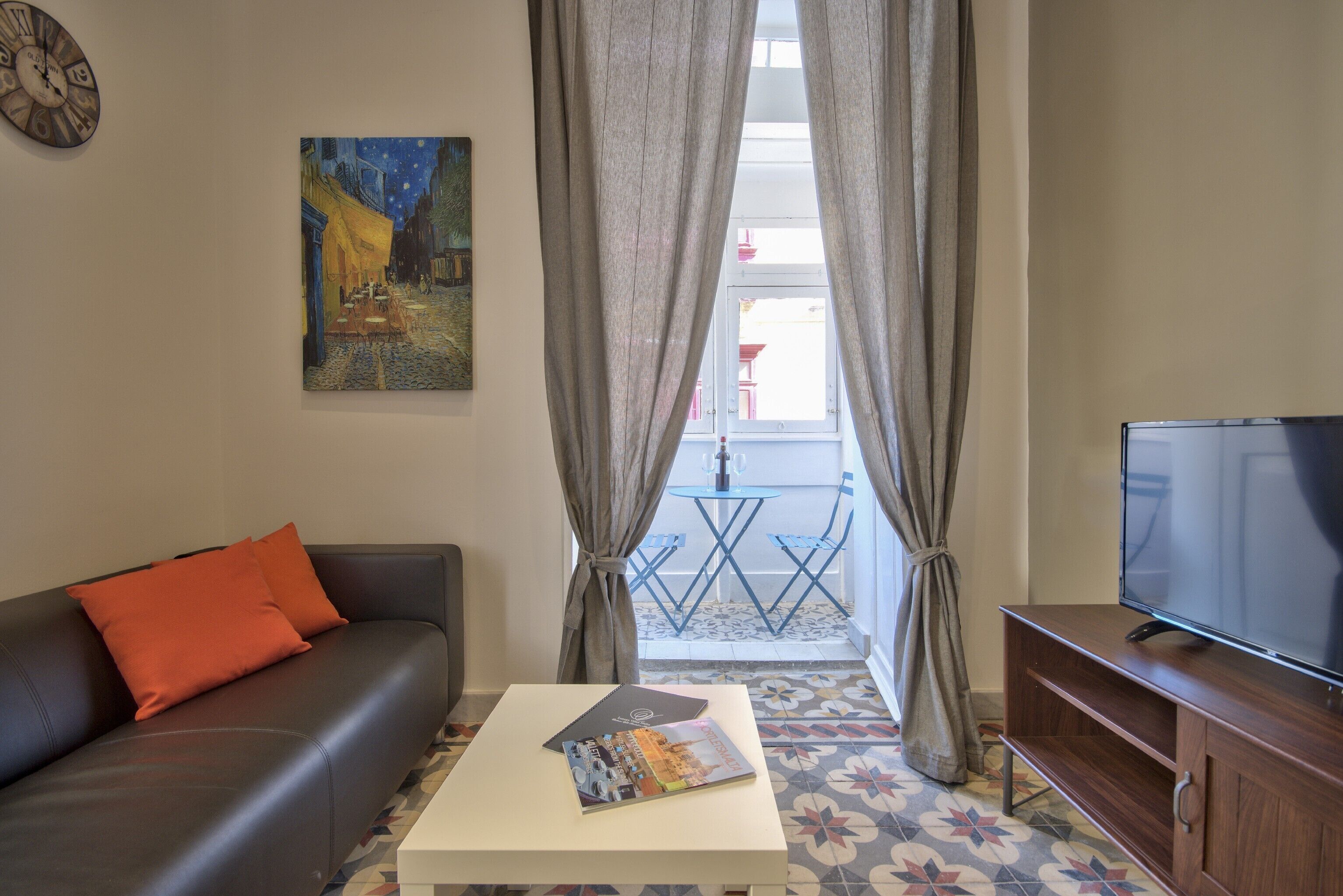 Uma sala de estar com um sofá, uma mesa de centro com uma revista, uma televisão e um quadro na parede.